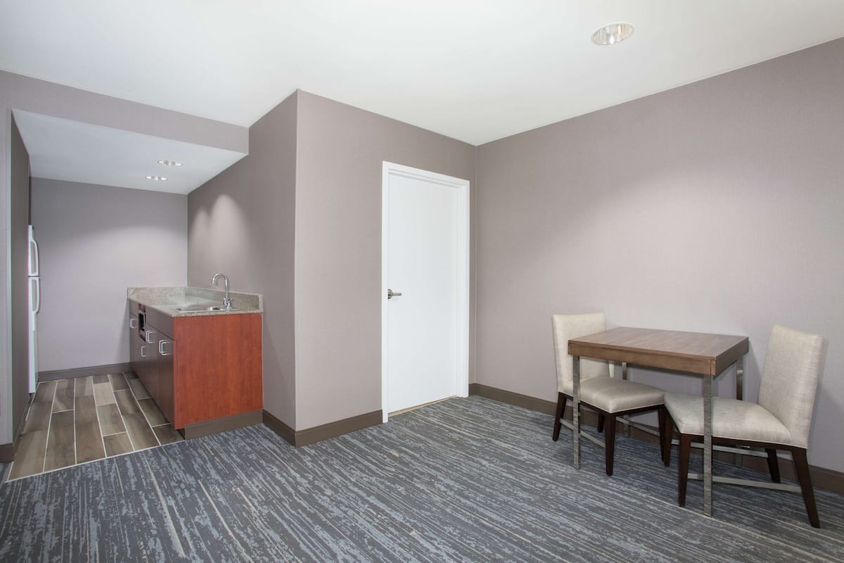 Quarto de hotel com cozinha compacta, mesa de jantar e cadeiras, e uma porta.
