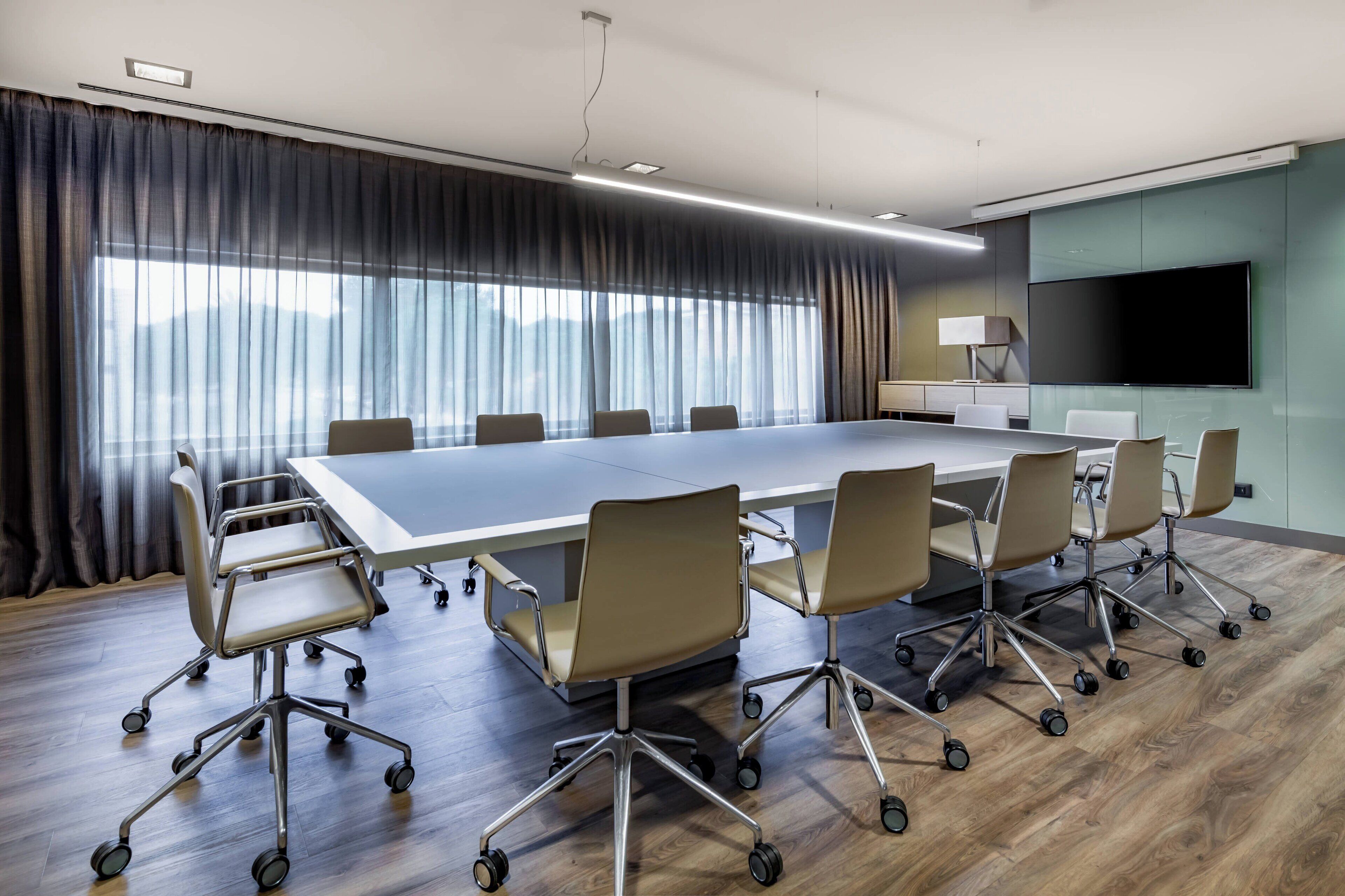 Sala de conferência com uma grande mesa, cadeiras, uma televisão e vista para o exterior.