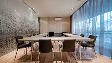 Uma sala de conferências com uma mesa comprida, cadeiras modernas e janelas amplas.