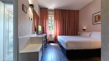 Quarto de hotel com cama, escrivaninha, cadeira, televisão e janela com cortinas.
