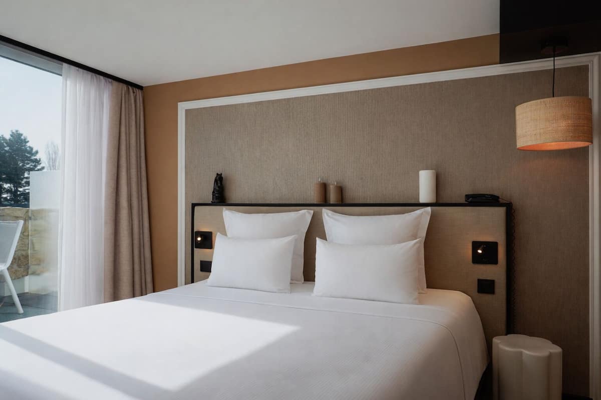 Quarto de hotel com uma cama grande, cabeceira com prateleira, luminárias de cabeceira e vista pela janela.