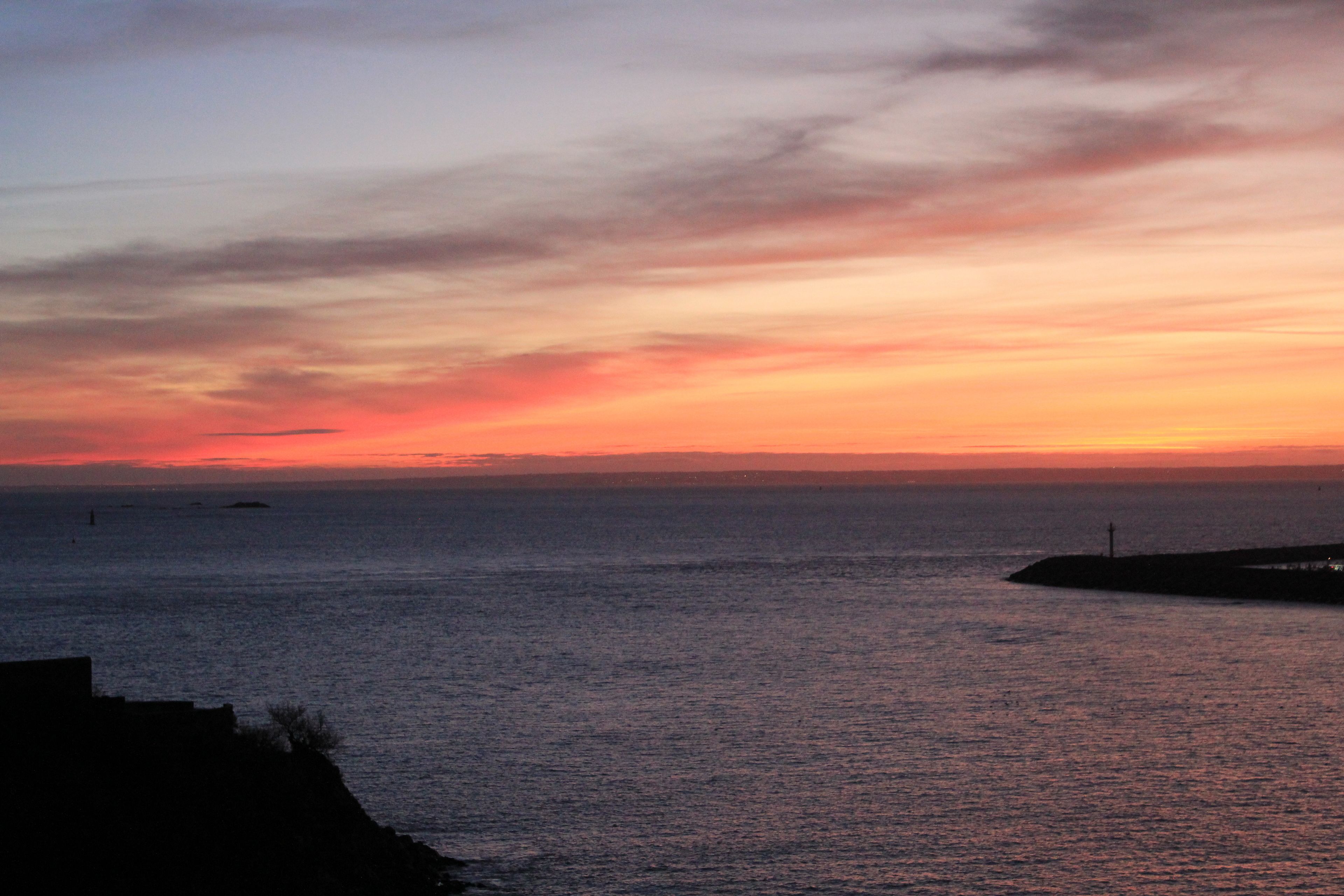 Um pôr do sol sobre um mar calmo com uma linha de costa distante.