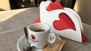 Uma xícara branca com uma colher e um saquinho de açúcar sobre uma mesa com um descanso trançado.