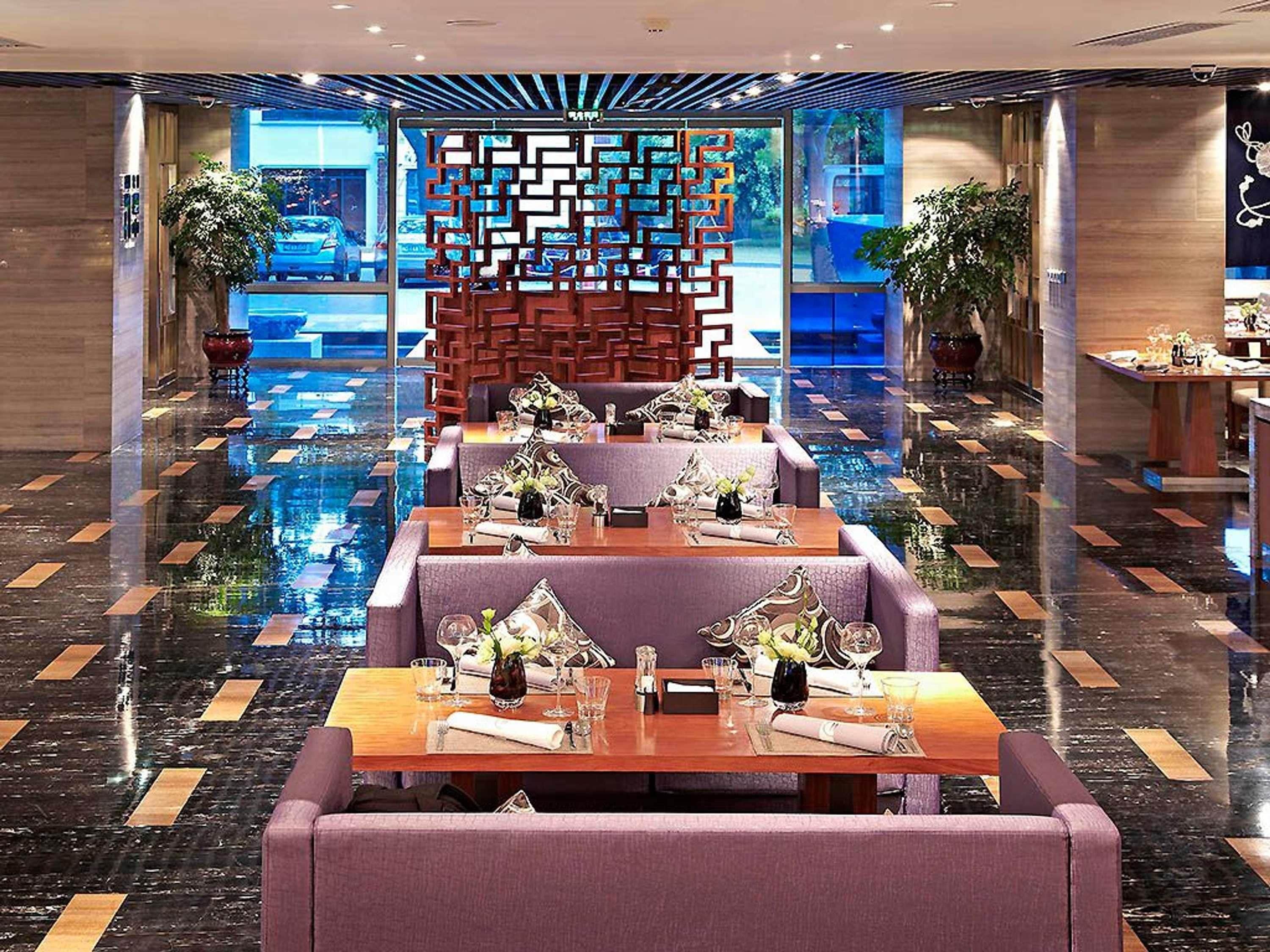 Um lobby de hotel com um recurso central de água, áreas de estar e uma parede decorativa.