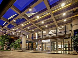 Um edifício moderno com fachada de vidro, entrada destacada e teto com padrões geométricos.