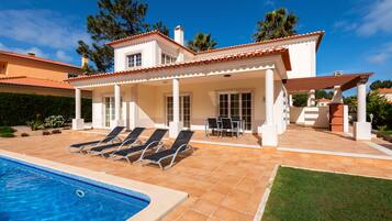 Uma casa de dois andares com piscina, varanda coberta com cadeiras de descanso e gramado bem cuidado.