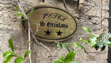 Placa de hotel antiga com o nome "HOTEL S. Grolano" e dois estrelas, fixada numa parede de pedra com plantas trepadoras.