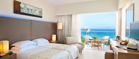 Quarto de hotel com duas camas, uma escrivaninha, uma cadeira e vista para o oceano.