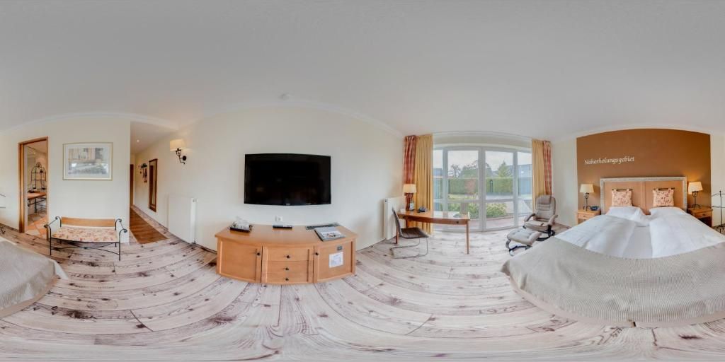 Vista panorâmica de um quarto de hotel com televisão, um armário de madeira, uma cama e uma área de jantar com mesa e cadeiras.