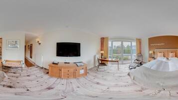 Vista panorâmica de um quarto de hotel com televisão, um armário de madeira, uma cama e uma área de jantar com mesa e cadeiras.