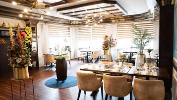 Interior de restaurante com piso de madeira, mesas redondas e cadeiras.