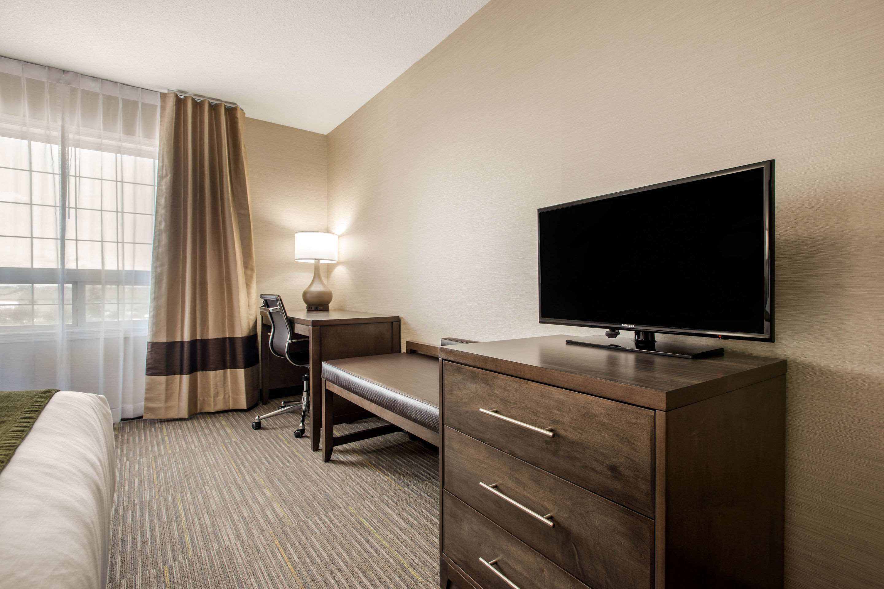 Quarto de hotel com cama, escrivaninha, televisão e abajur.