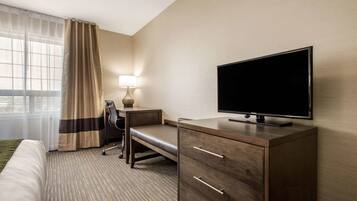 Quarto de hotel com cama, escrivaninha, televisão e abajur.