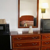 Quarto de hotel com cômoda de madeira, televisão, micro-ondas e cama com colcha florida.