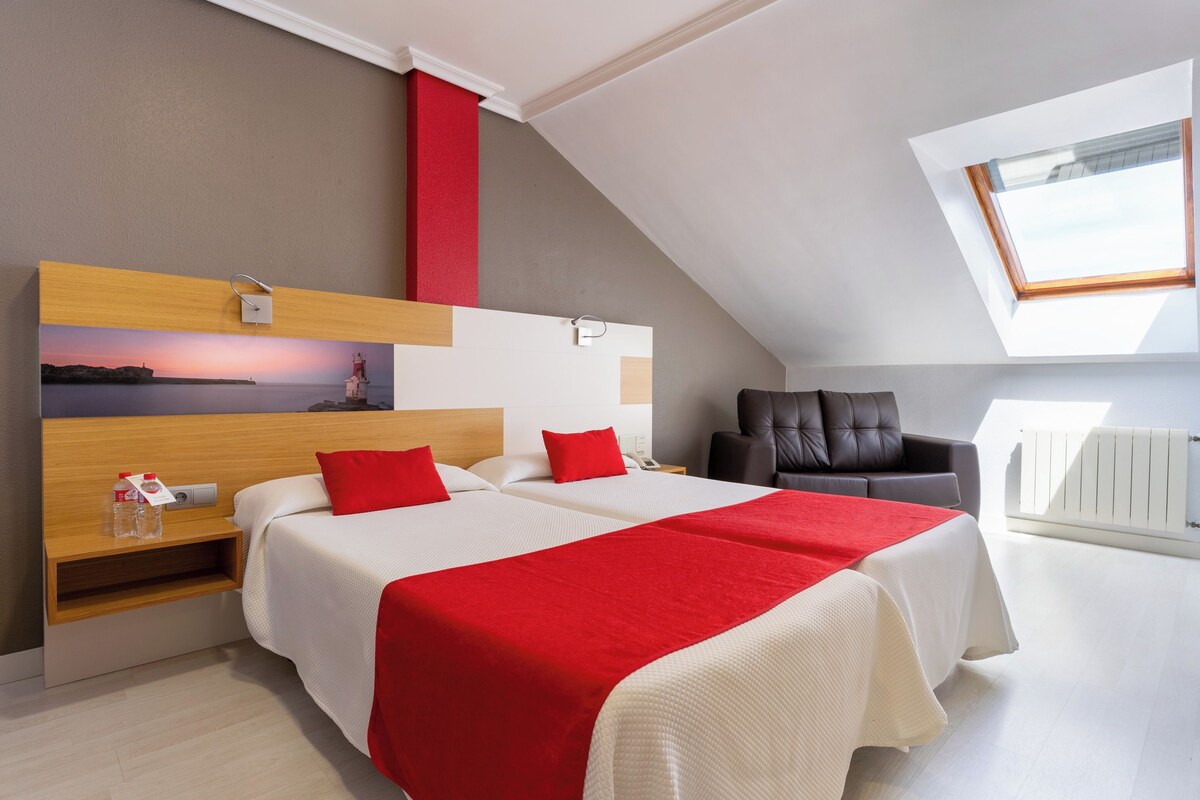 Quarto de hotel moderno com duas camas, uma parede de destaque vermelha, uma janela grande e vista para o mar.