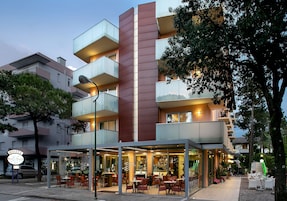 Um hotel moderno com fachada de vidro, área de estar externa e bar à vista.