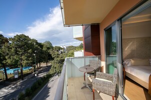 Varanda com mesa e cadeiras, uma cama com cabeceira e vista para uma piscina e árvores.