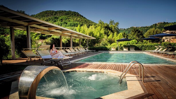 Uma área de piscina com espreguiçadeiras, uma banheira de hidromassagem e um deck de madeira.