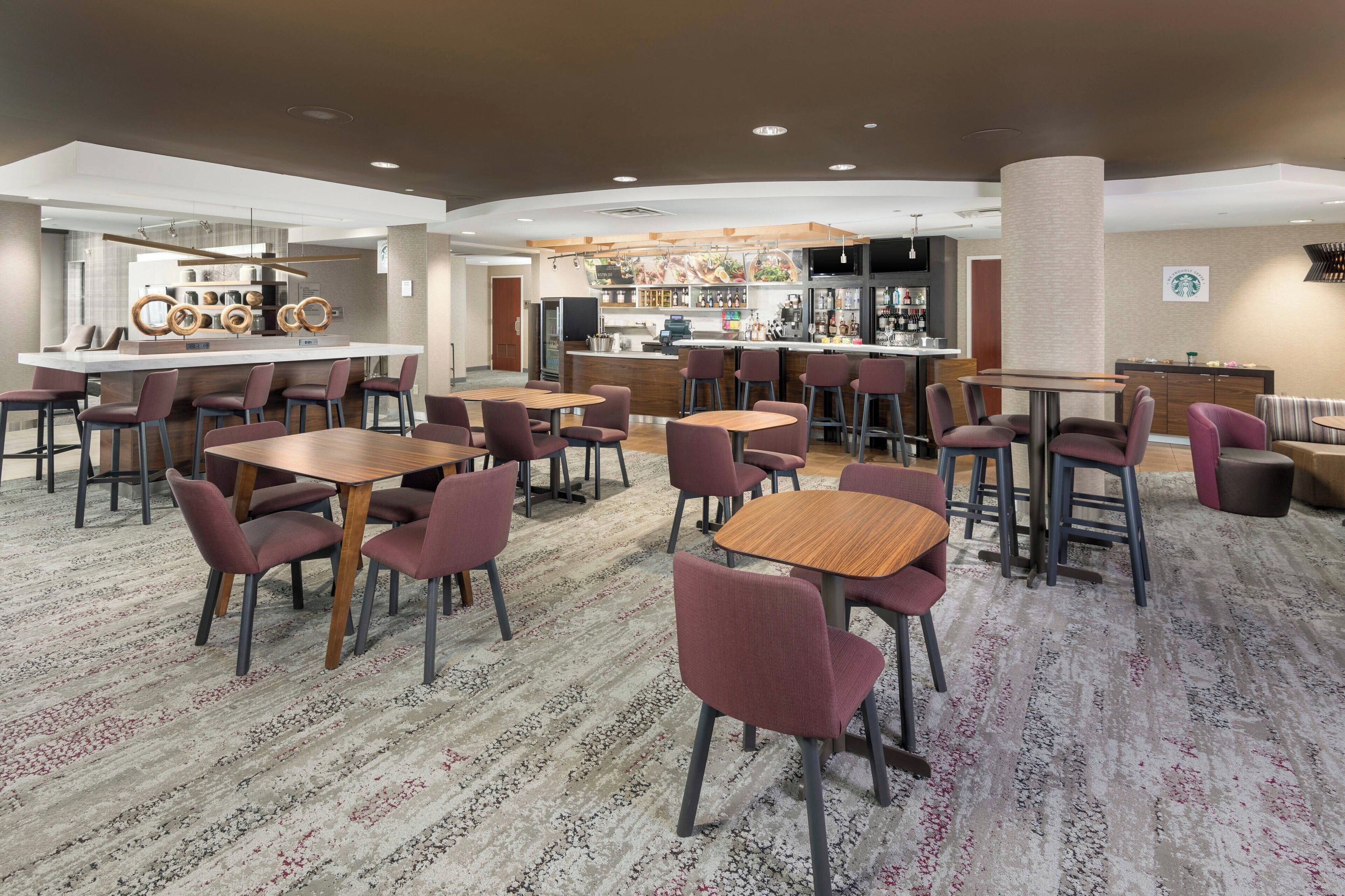 Um lobby de hotel moderno com área de bar, espaços de estar e carpete estampado.
