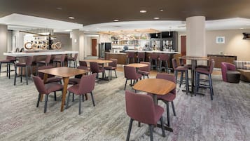 Um lobby de hotel moderno com área de bar, espaços de estar e carpete estampado.