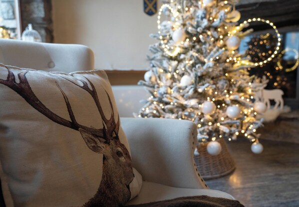 Um quarto aconchegante com uma poltrona confortável, um travesseiro de veado, uma árvore de Natal decorada e uma lareira.