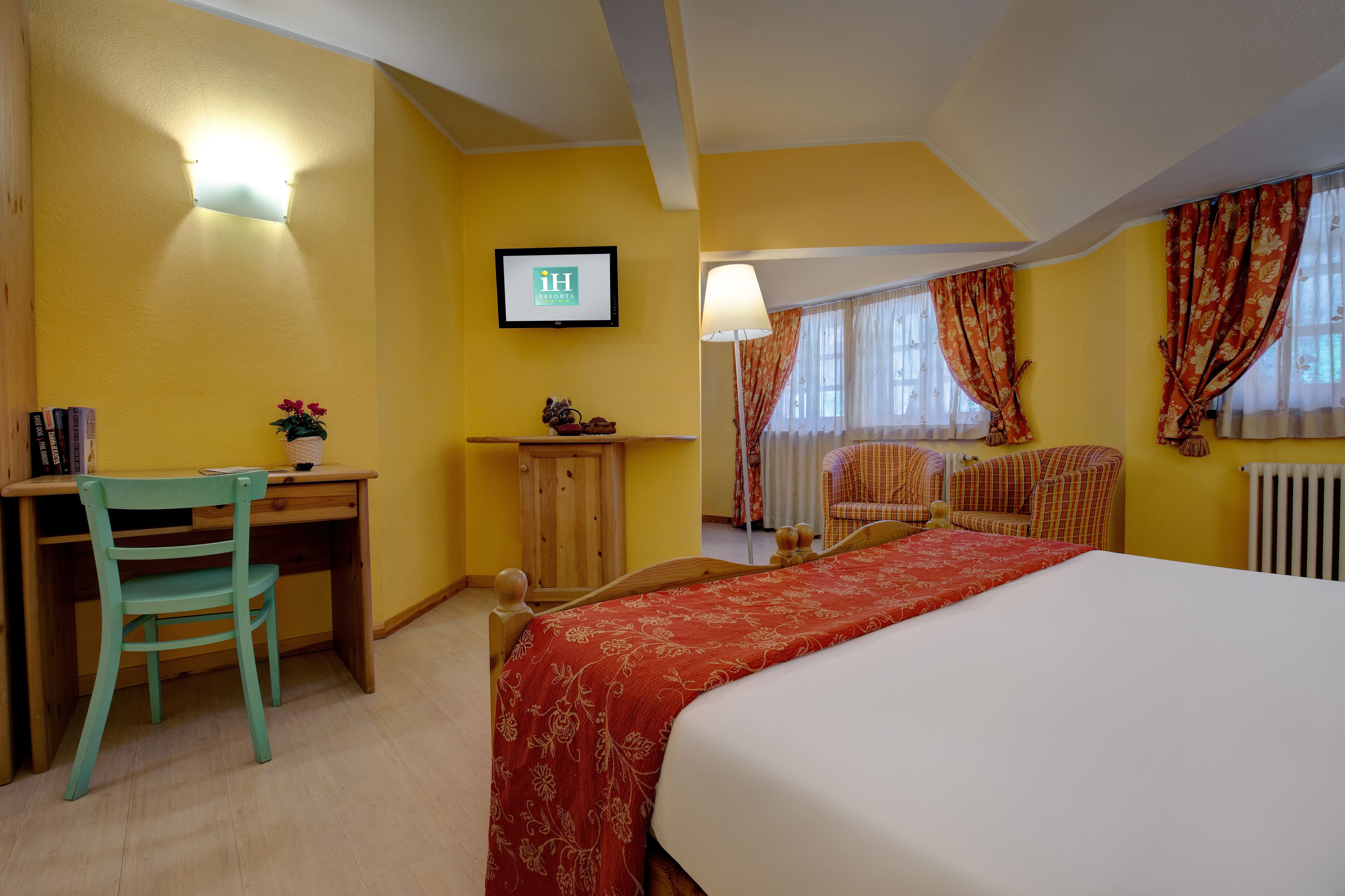 Quarto de hotel com cama, escrivaninha, cadeira e janela com cortinas.
