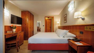 Quarto de hotel com uma cama, uma escrivaninha com computador, televisão e telefone.
