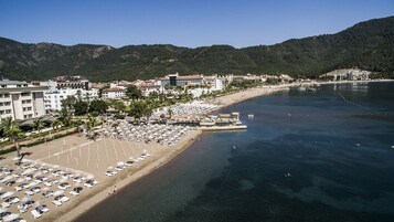 Uma área costeira com uma praia, um porto de iates e edifícios ao fundo.