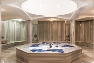 Um banheiro luxuoso com uma grande banheira de mármore, um espelho redondo e um lustre no teto.