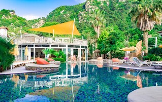 Uma área de piscina com espreguiçadeiras e um bangalô, cercada por vegetação exuberante e montanhas ao fundo.