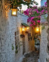 Uma estreita passagem de pedra com a entrada de um hotel boutique, iluminada por lanternas penduradas e trepadeiras floridas.