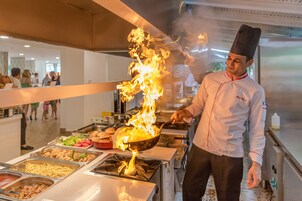 Um chef realizando um flambé com um wok em um buffet.