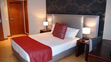 Quarto de hotel com uma cama grande, duas mesas de cabeceira com luminárias, uma porta de madeira e parede com padrão.