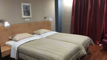 Uma cama de casal com cabeceira de madeira, duas luminárias de cabeceira, um criado-mudo, um quadro na parede e uma cortina vermelha.