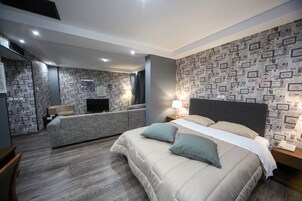 Quarto de hotel moderno com uma cama grande, um sofá, uma TV e uma parede decorada com quadros.