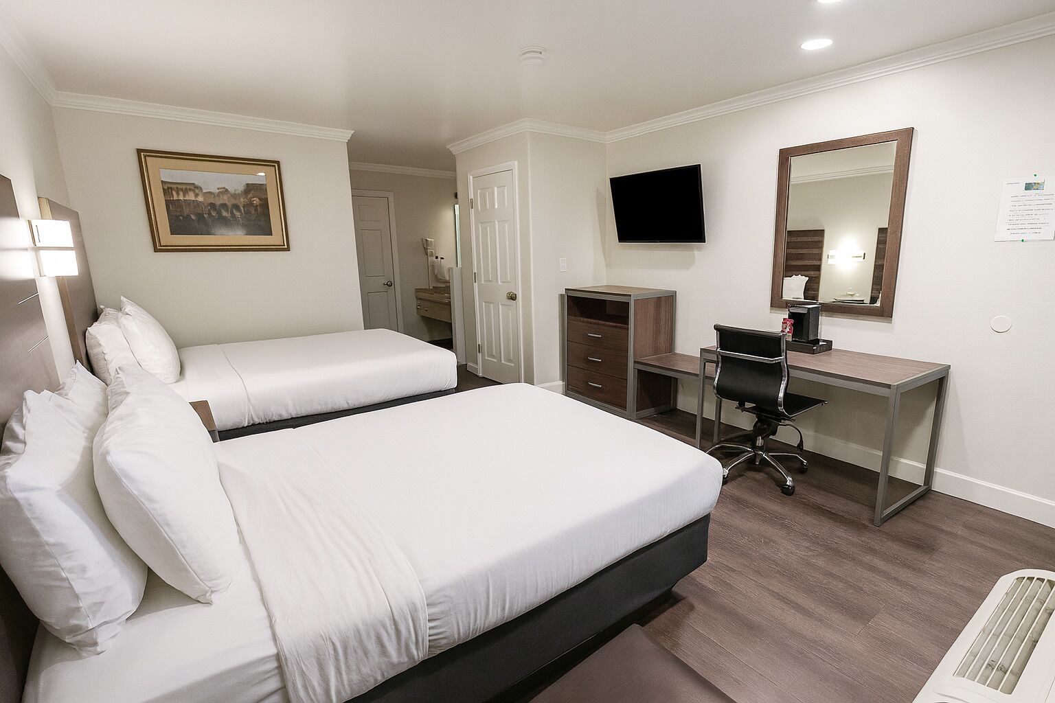 Quarto de hotel com duas camas, uma escrivaninha, uma cadeira, uma televisão e um espelho.