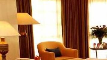 Quarto de hotel com cama, escrivaninha com luminária, cadeira e janela com cortinas.