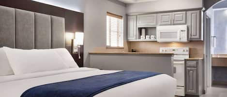 Quarto de hotel com cama, escrivaninha, micro-ondas e uma pequena copa.