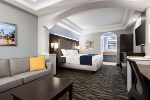 Quarto de hotel com cama, sofá, escrivaninha e televisão.
