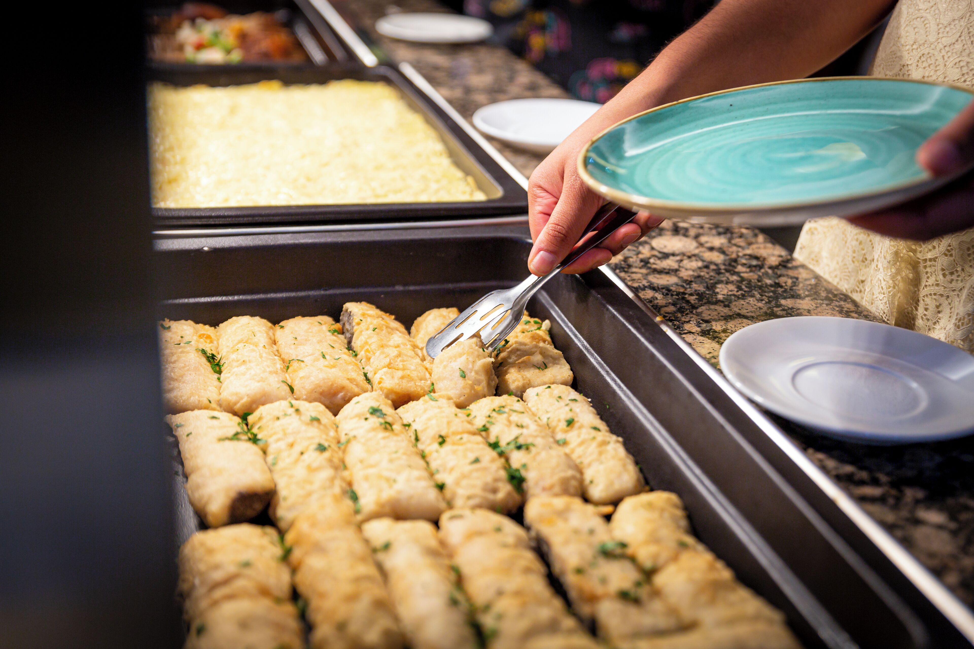 Buffet variado com diversas opções de comida, incluindo uma bandeja de aperitivos enrolados e decorados com ervas.