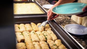 Buffet variado com diversas opções de comida, incluindo uma bandeja de aperitivos enrolados e decorados com ervas.