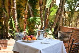 Uma mesa com uma fruteira, um balde de metal e um saca-rolhas, em ambiente externo com cadeiras e uma parede de tijolos.