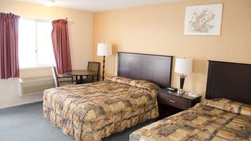 Quarto de hotel com uma cama grande, uma cama menor, uma escrivaninha com cadeira, duas luminárias de cabeceira e uma janela com cortinas.