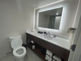 Casa de banho moderna com sanita branca, lavatório com espelho em cima e um porta-toalhas.