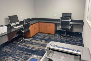 Uma sala de conferências com dois computadores de mesa, uma impressora e uma grande escrivaninha.