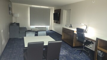 Quarto de hotel com cama, escrivaninha, cadeira, televisão e janela.