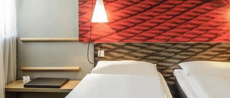 Quarto de hotel com duas camas, uma mesa de cabeceira, uma luminária e parede com textura.