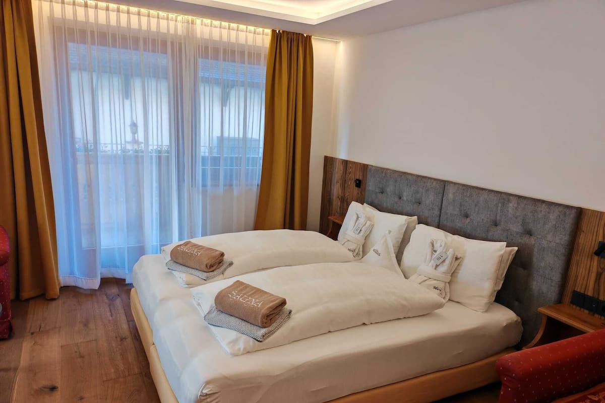 Uma cama de casal com roupa de cama branca e duas toalhas, uma cabeceira de madeira, uma mesa de cabeceira de madeira e uma poltrona vermelha.