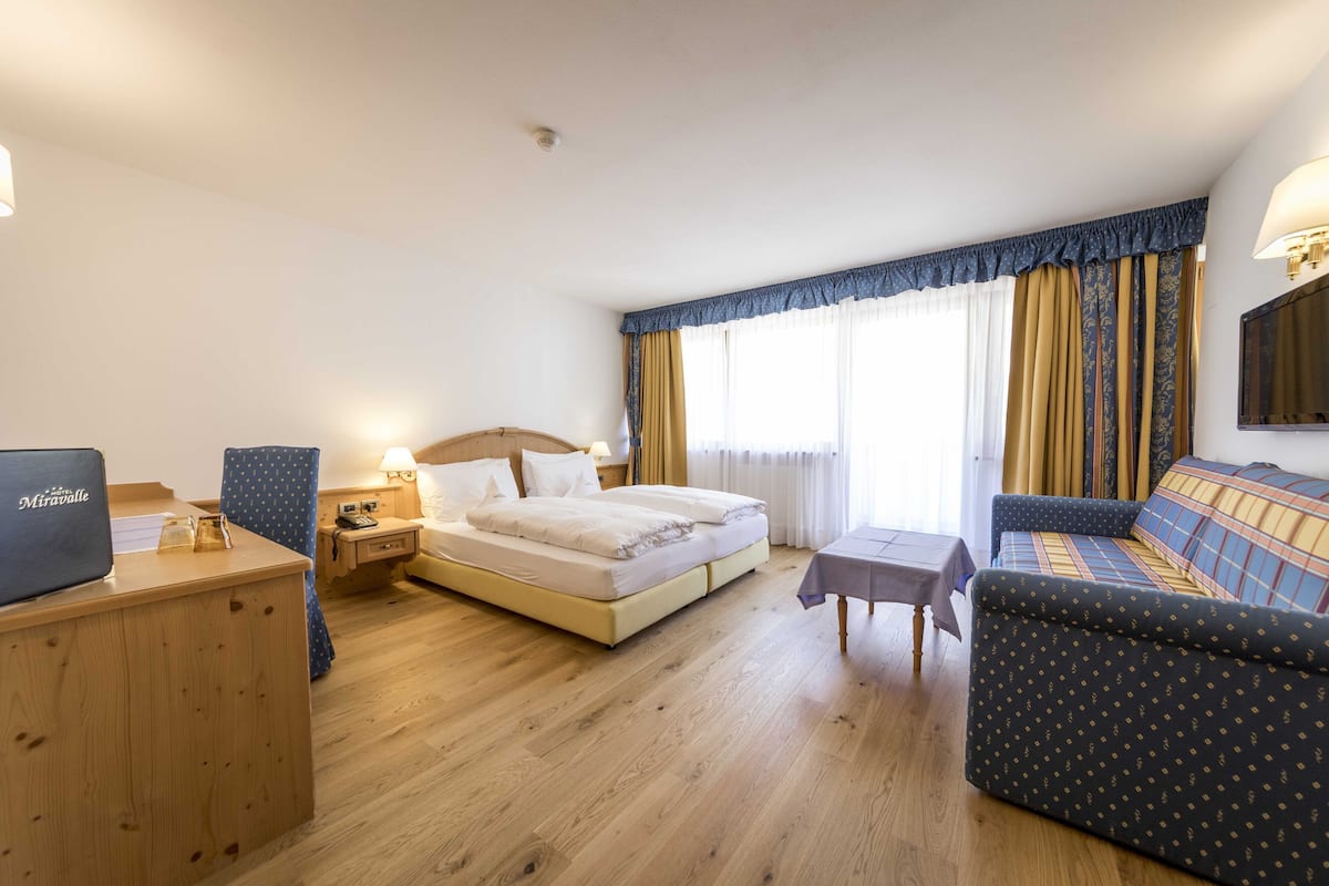 Quarto de hotel com cama, escrivaninha com laptop, cadeira, sofá e mesa pequena.