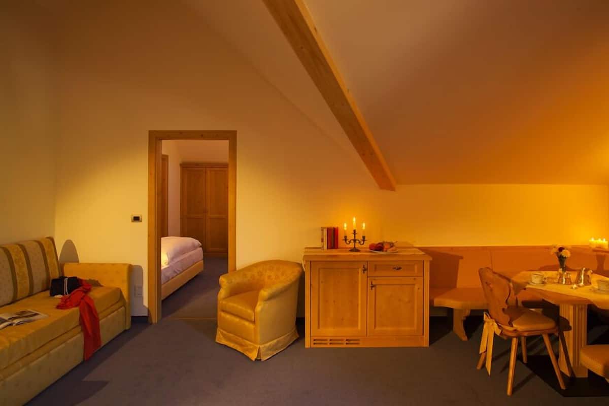 Quarto de hotel acolhedor com cama, sofá, poltrona pequena, armário de madeira e mesa de jantar com cadeiras.